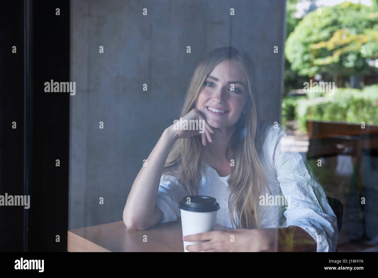Young smiling woman sitting in cafe with coffee photographed through ...
