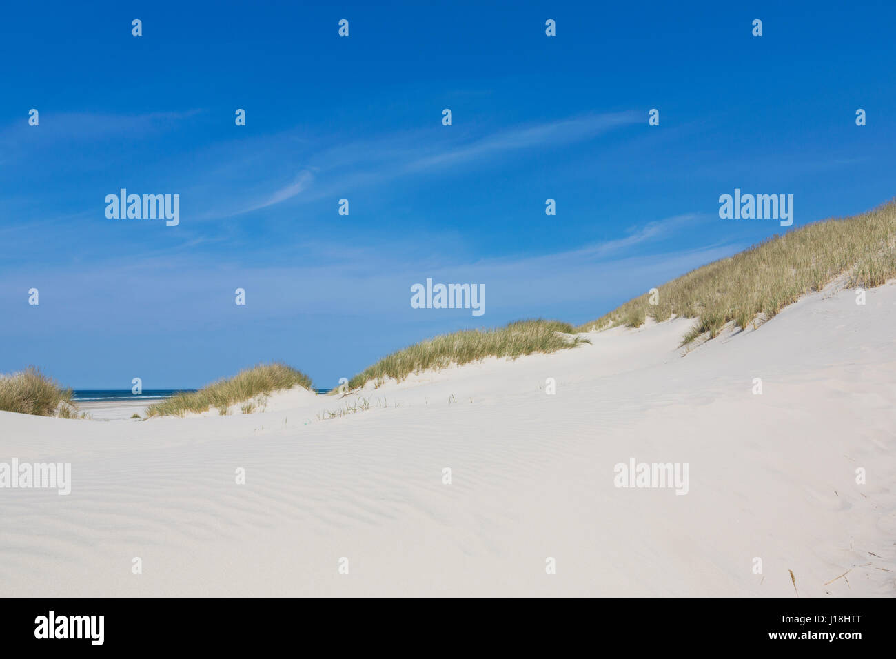 Sand dunes with grass against blue sky with clouds Stock Photo - Alamy