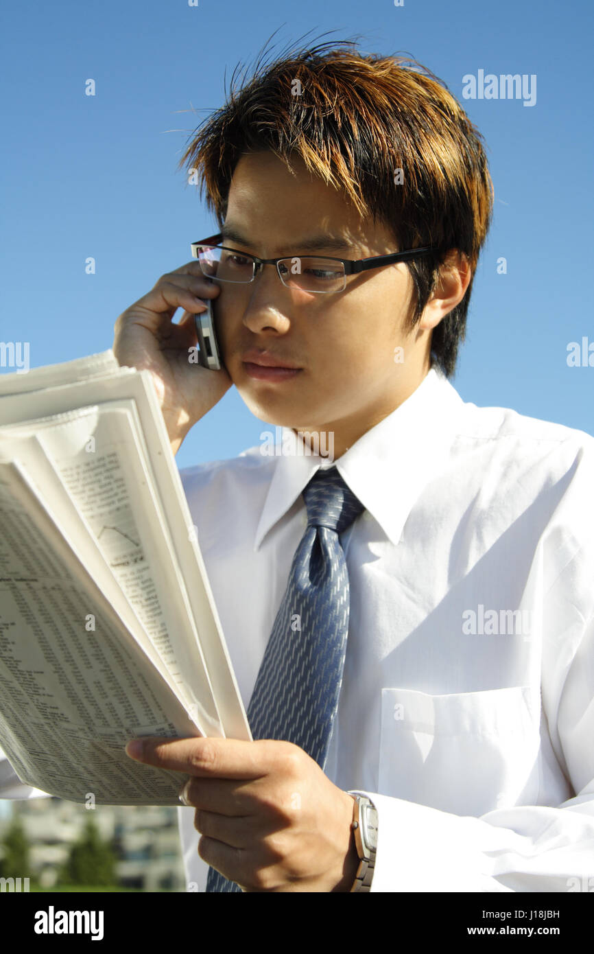 Businessman reading a financial newspaper while making a phone call ...