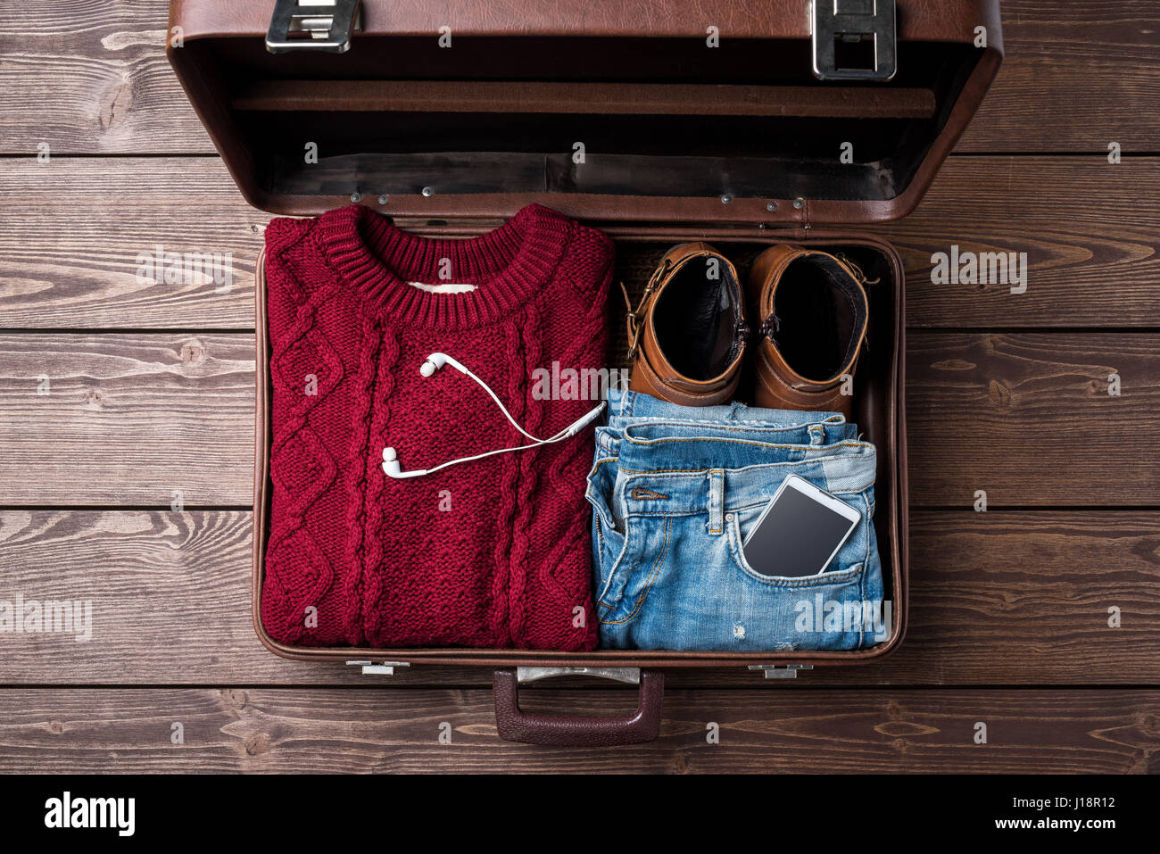 Open suitcase with casual female winter clothes on wooden table. Top ...