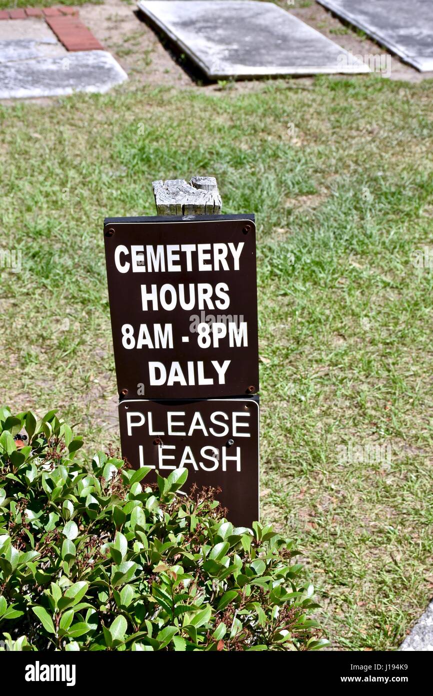 Cemetery hours sign with graves in the background Stock Photo - Alamy