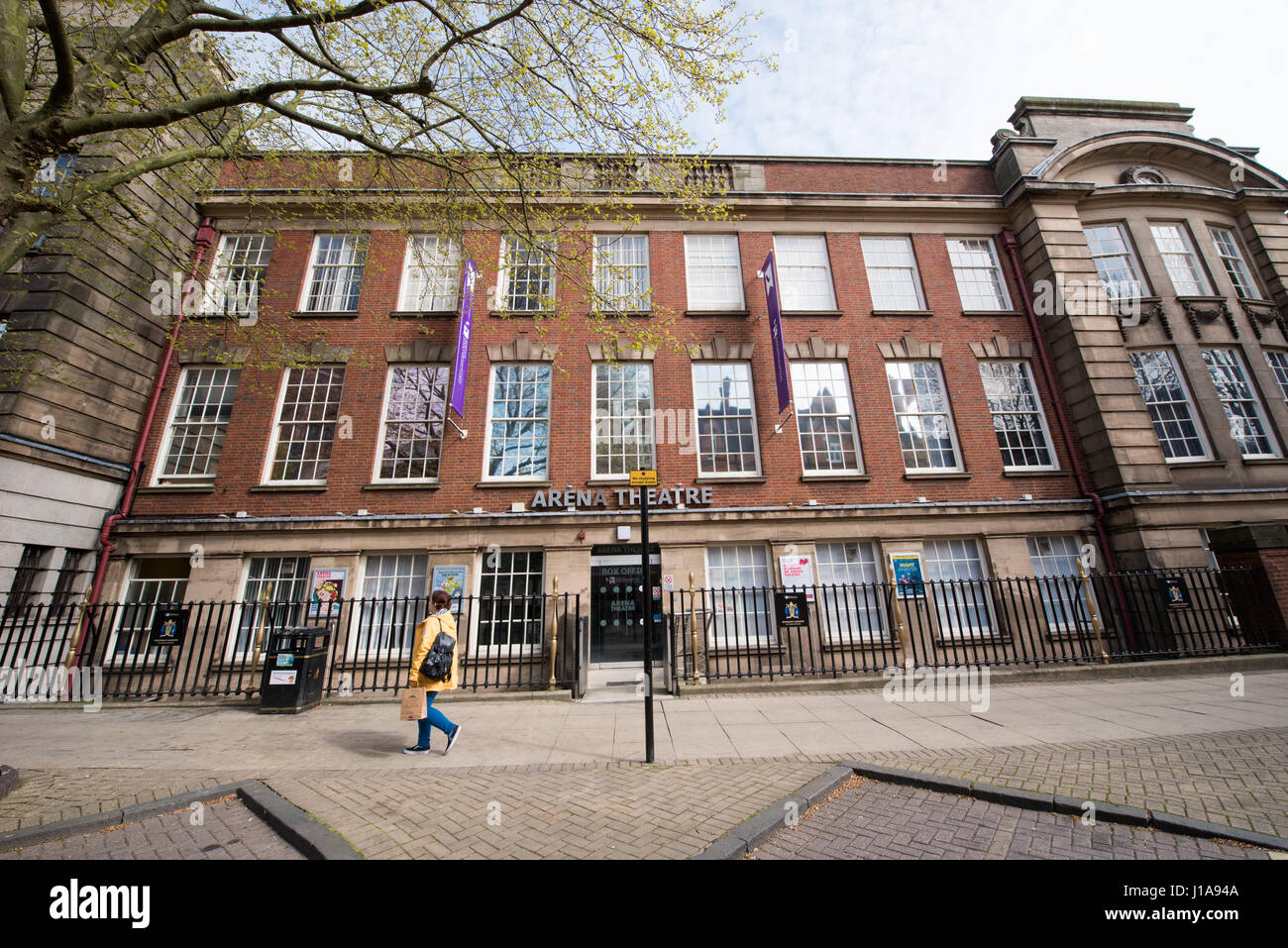 Woman in a yellow coat walking past the entrance to the popular Arena ...