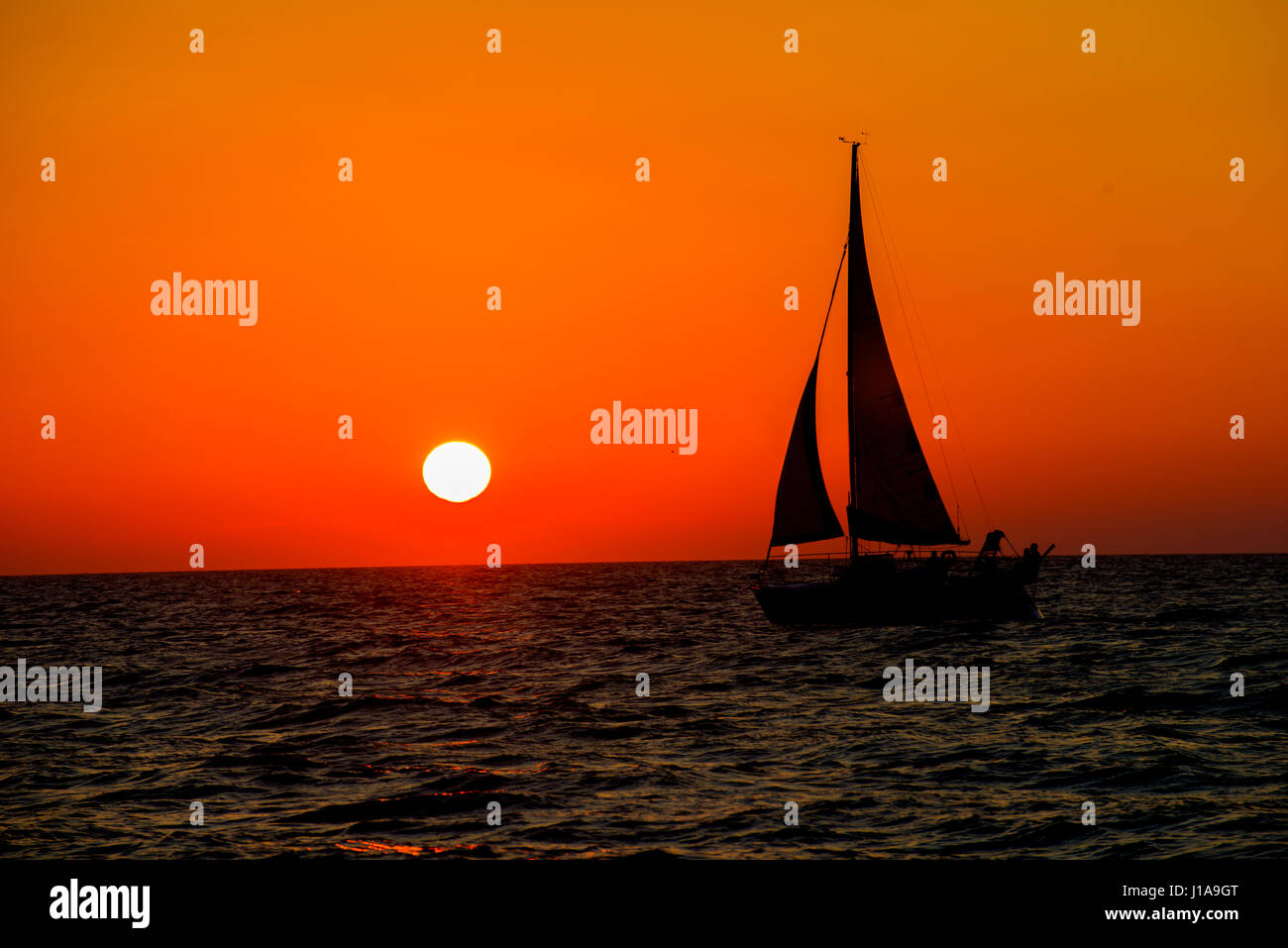 sailboat sailing into sunset on ocean Stock Photo - Alamy