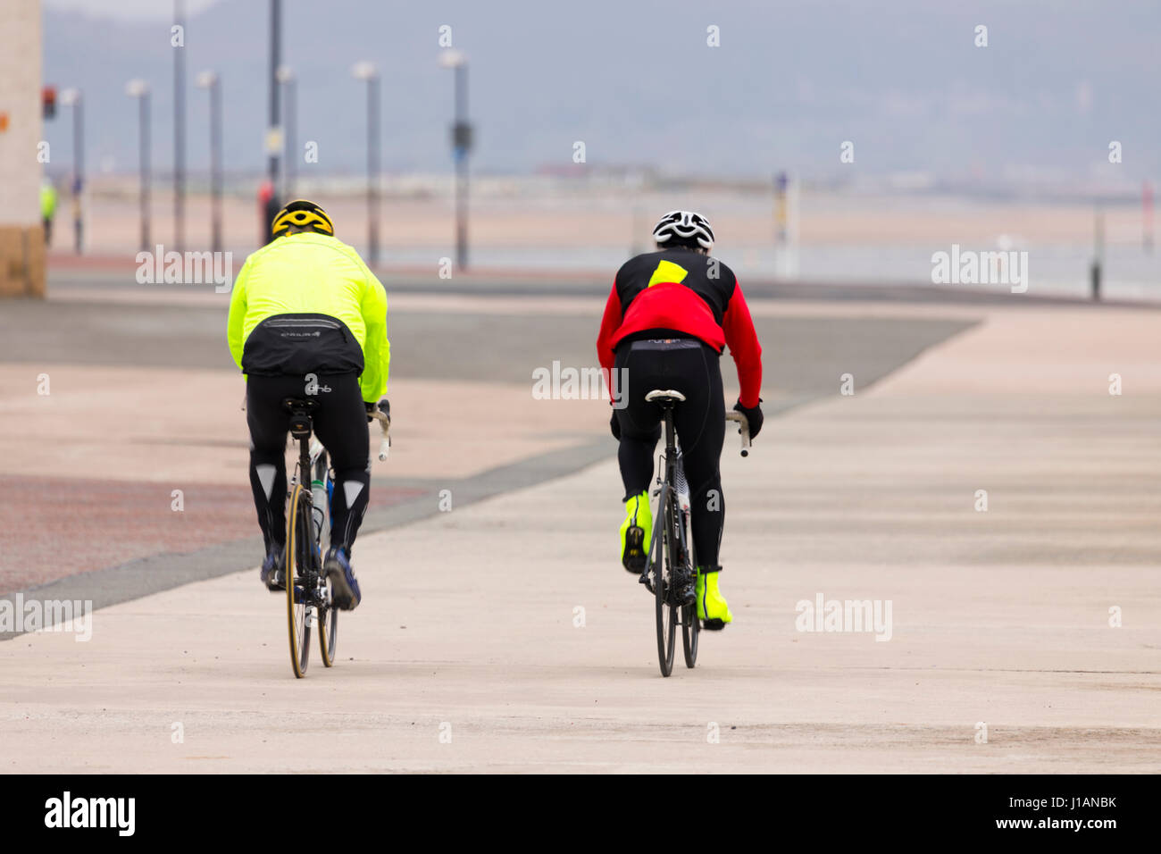 Two men cycling together along the coastal seafront and promenade of ...