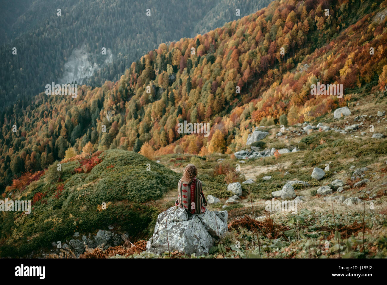 Caucasian woman sitting on mountain rock overlooking valley Stock Photo ...