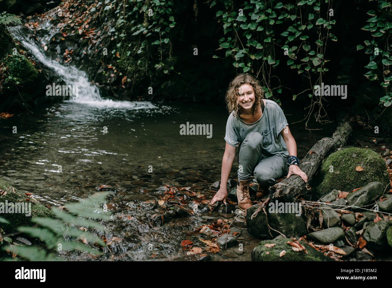 Caucasian woman crouching on rock in forest stream Stock Photo - Alamy