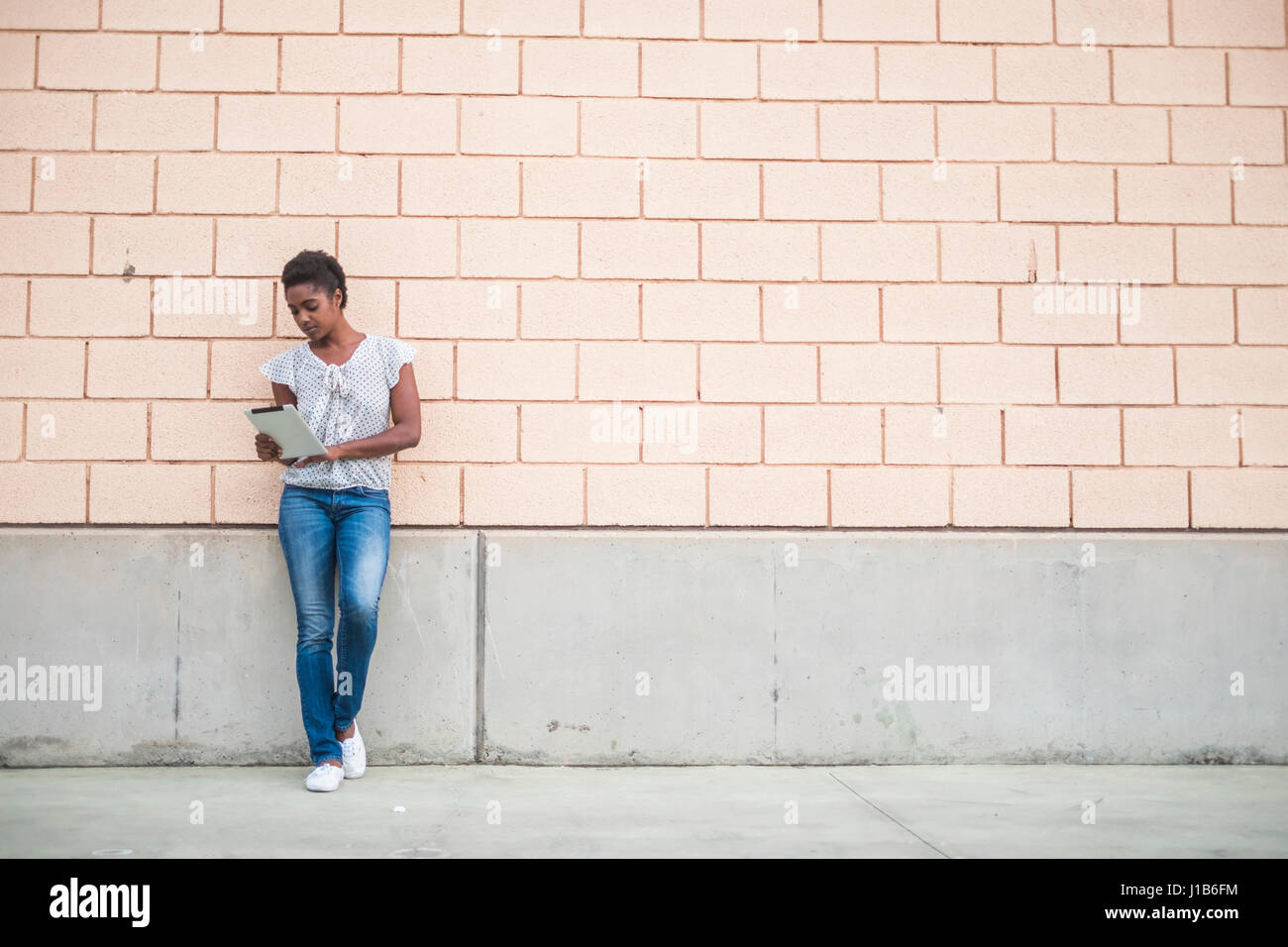 African American woman leaning on concrete wall using digital tablet ...
