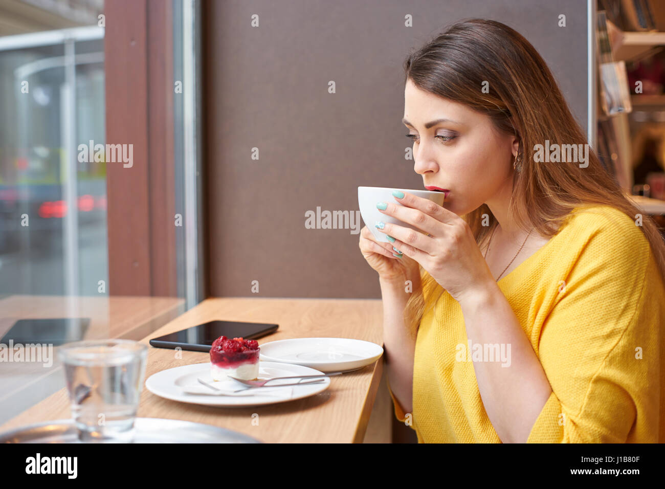 A young woman is taking a sip of coffee at the table with raspberry ...