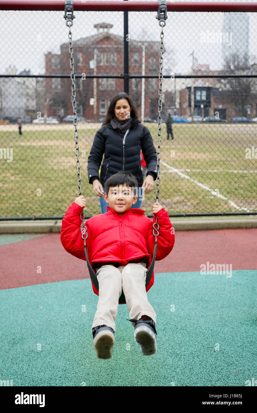 Mother pushing son on swing at playground Stock Photo - Alamy