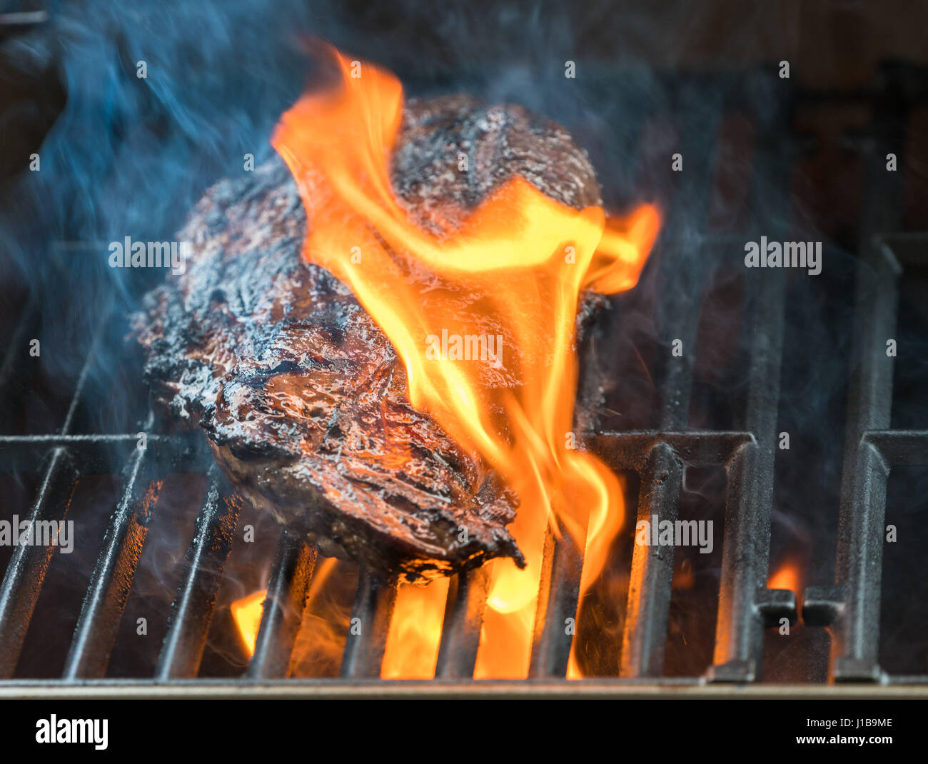 Cooking food on a BBQ - Close up of large piece of beef steak flaming ...