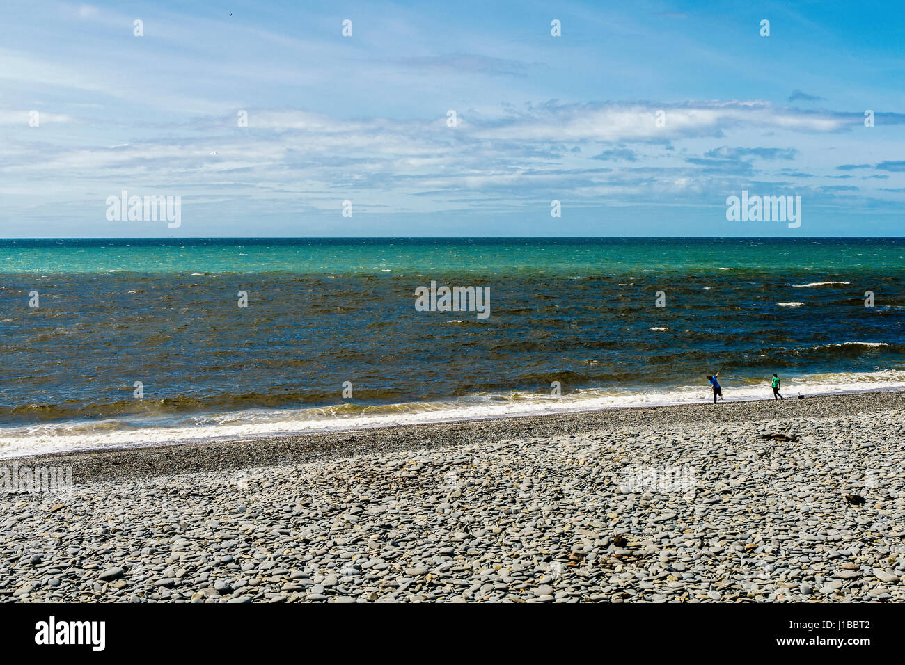 Two teenage boys playing and skimming pebbles on the beach in ...