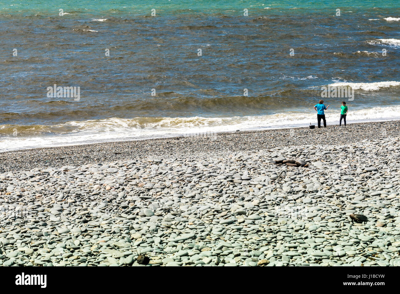 Two teenage boys playing and skimming pebbles on the beach in ...