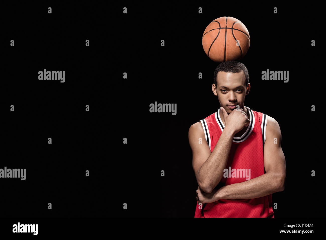 Young smiling basketball player standing with ball on head on black ...