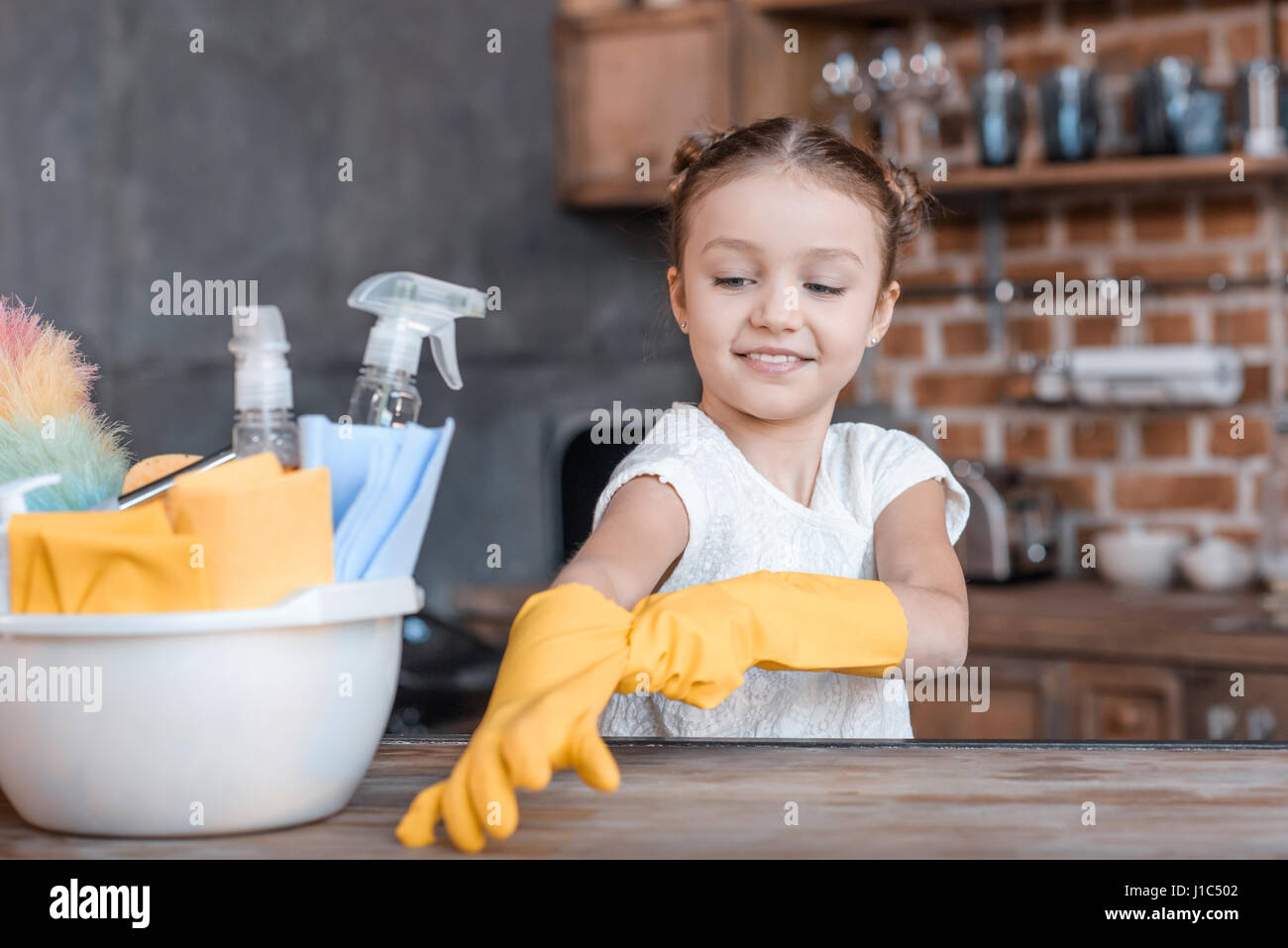 Adorable girl with rubber gloves and different cleaning supplies at ...