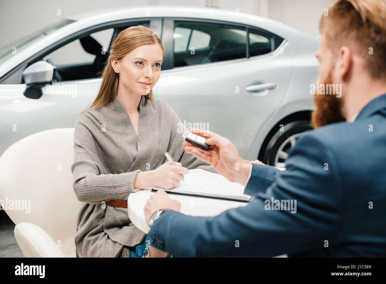 Bearded salesman giving new car key to young woman signing papers Stock ...