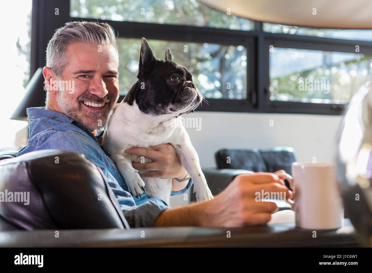 Caucasian man hugging dog on sofa and drinking coffee Stock Photo - Alamy