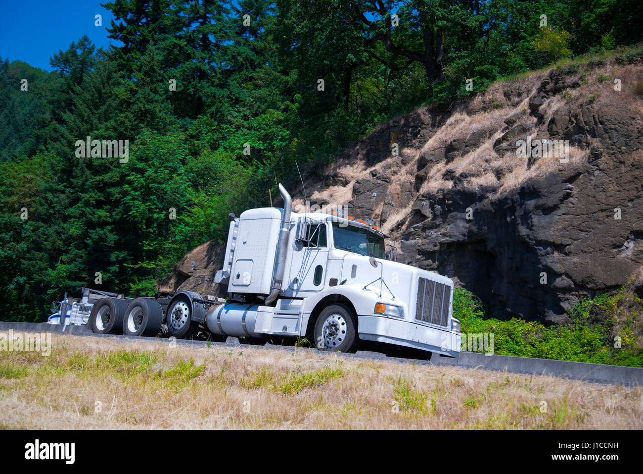 Powerful white semi truck with a flat bed trailer moving on the green ...