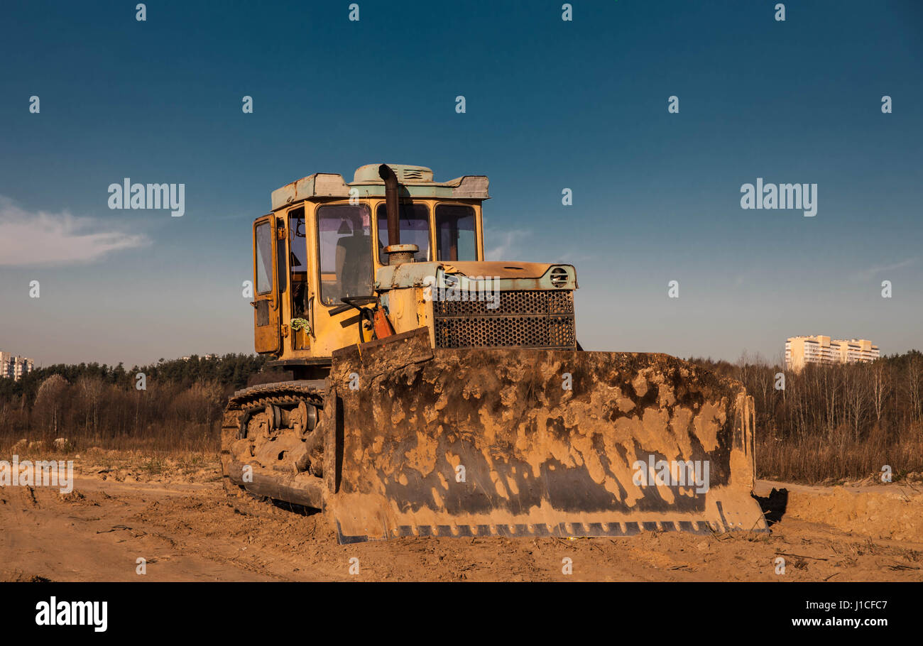Old yellow bulldozer on the road construction site on sunset Stock ...