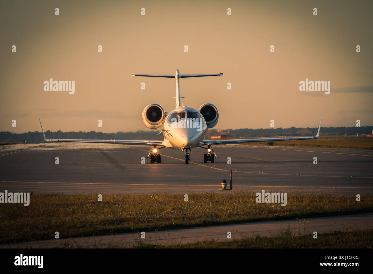 Business jet taxiing along the runway in the airport on sunset Stock ...
