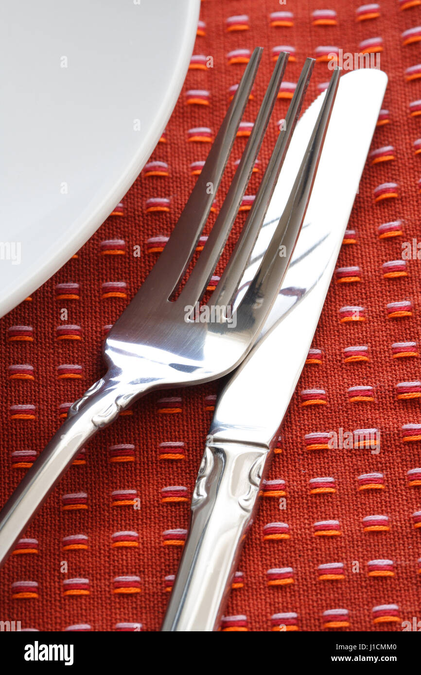 A shot of a dining table with plate, fork and knife on a red tablecloth ...