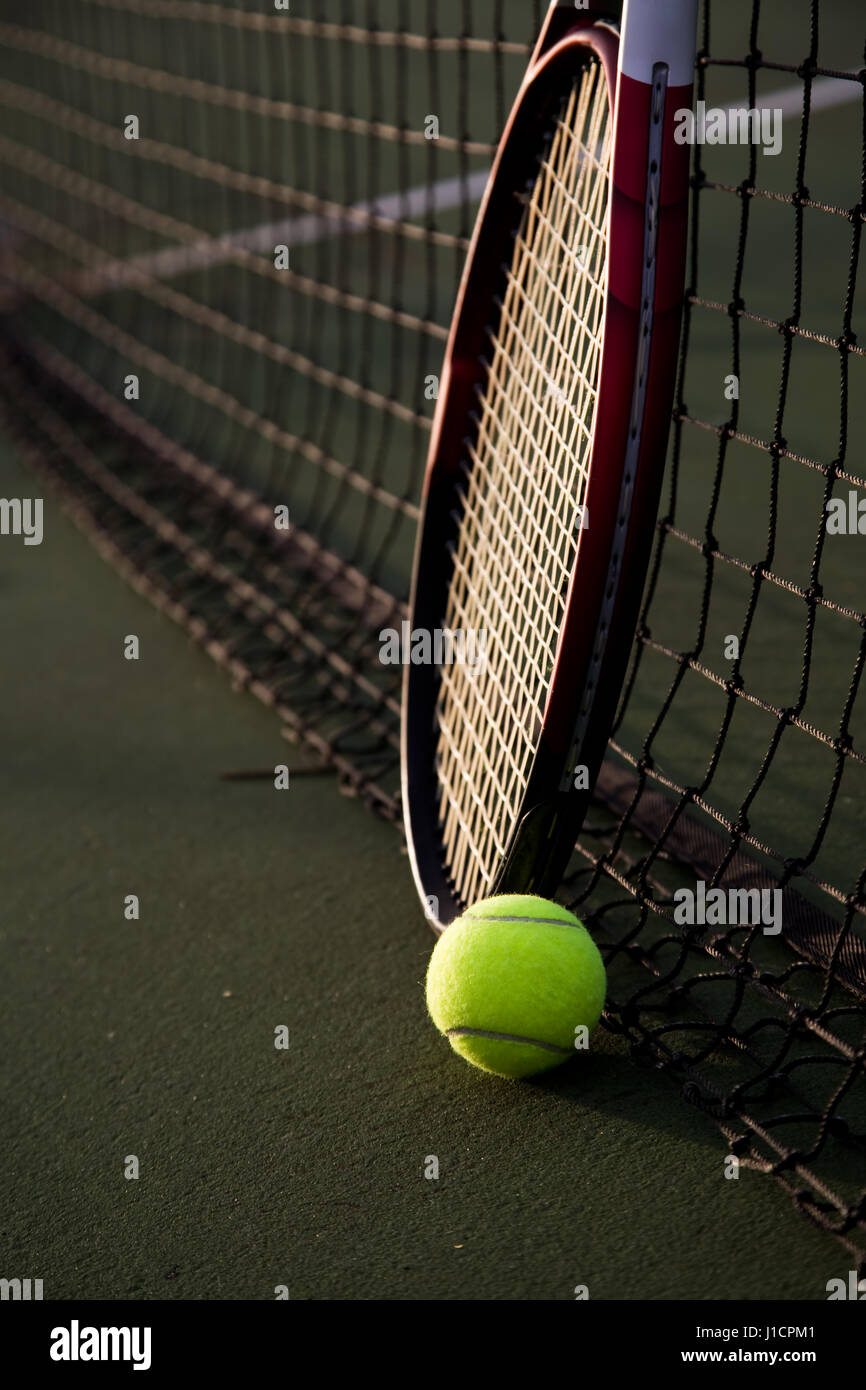 A shot of a tennis racquet and a tennis ball leaning against the net on ...