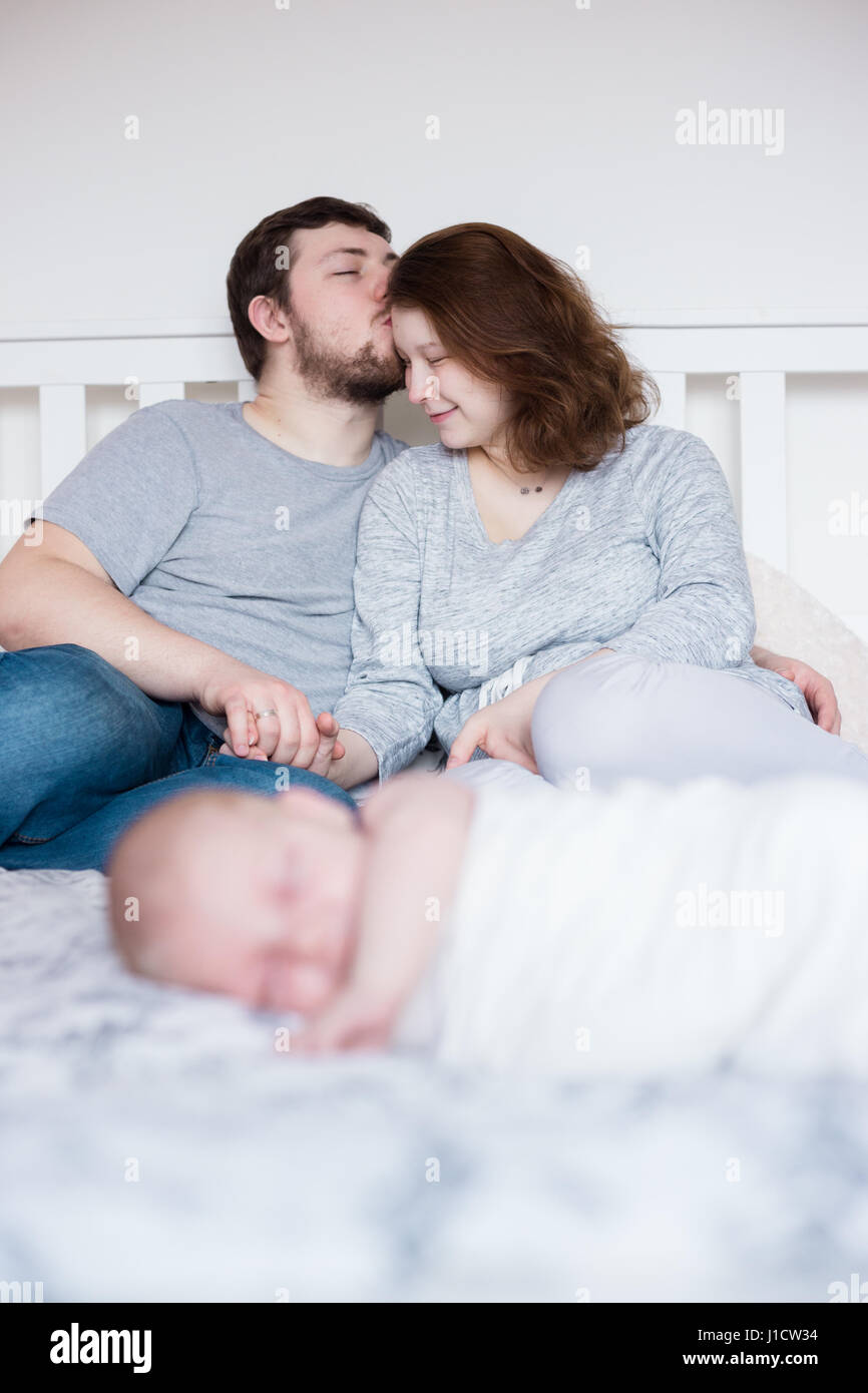 Young parents resting in bed, their newborn daughter sleeping in th e ...