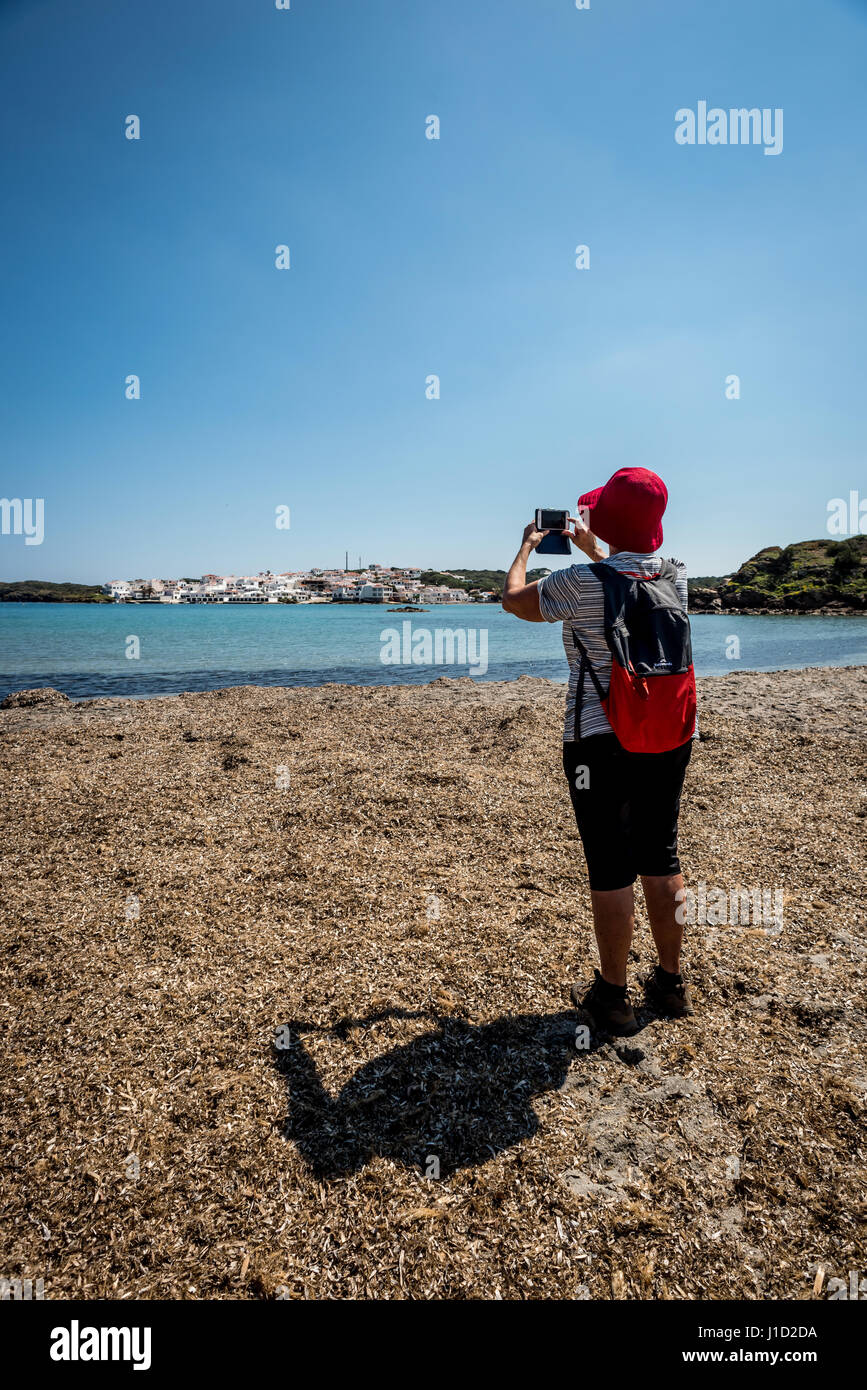A woman taking a photograph across the bay at Es Grau, Menorca Stock ...