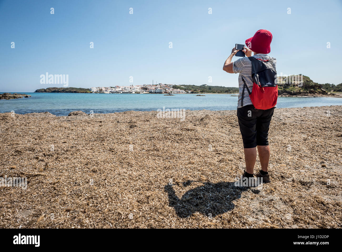 A woman taking a photograph across the bay at Es Grau, Menorca Stock ...