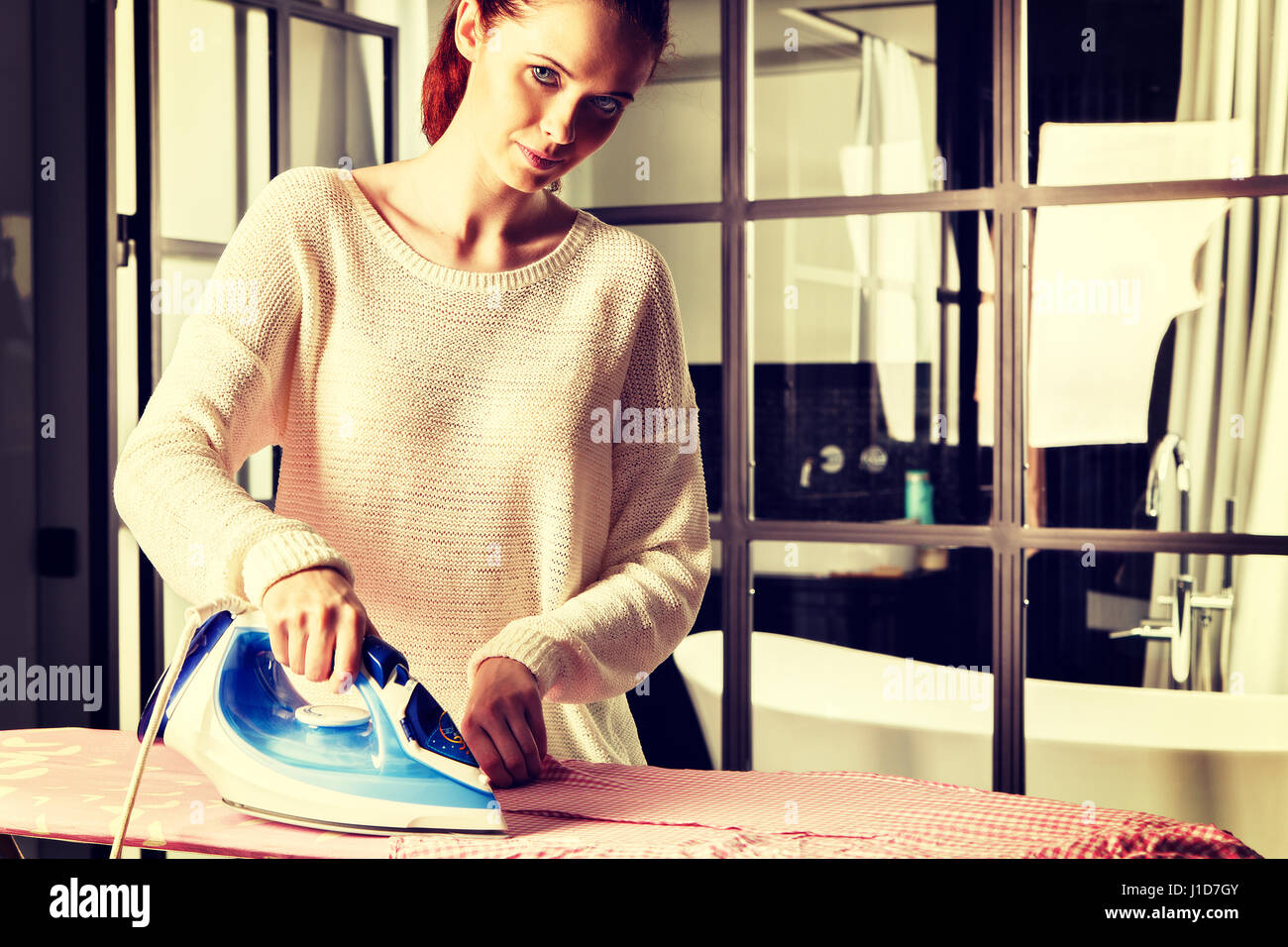 Red-haired young beautiful woman ironing clothes. Housework concept ...