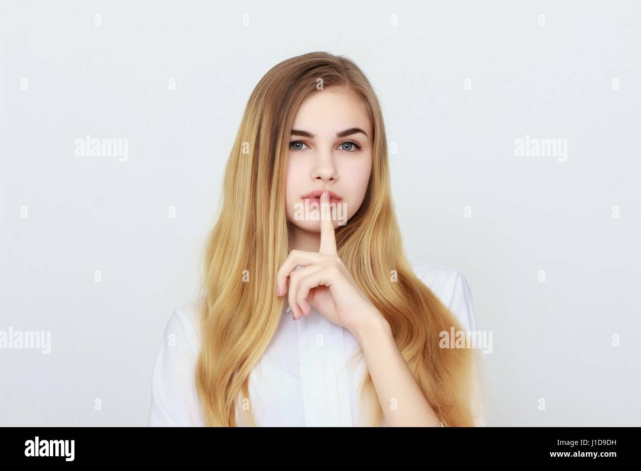 Portrait of young woman keeping finger on her lips and asking to keep ...