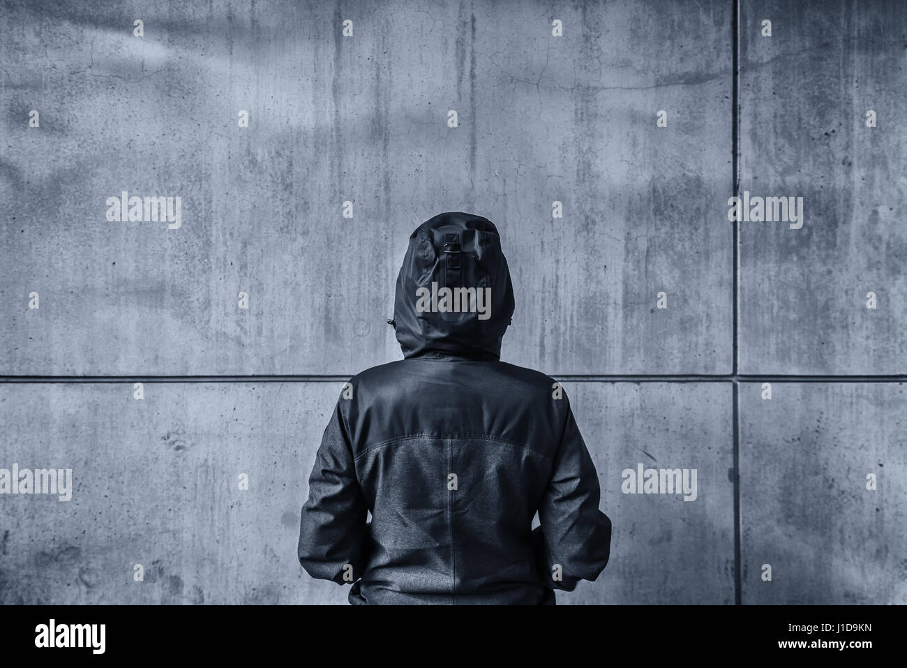 Unrecognizable hooded female person facing concrete wall as ...