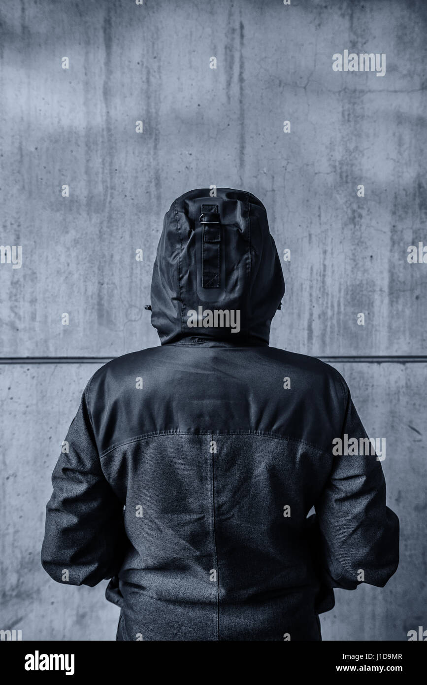 Unrecognizable hooded female person facing concrete wall as ...