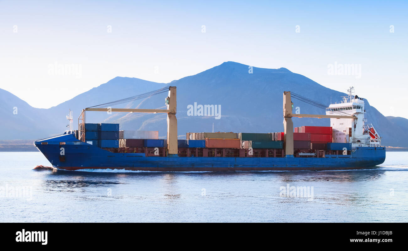 Container ship goes on Norwegian sea with mountains on a background ...