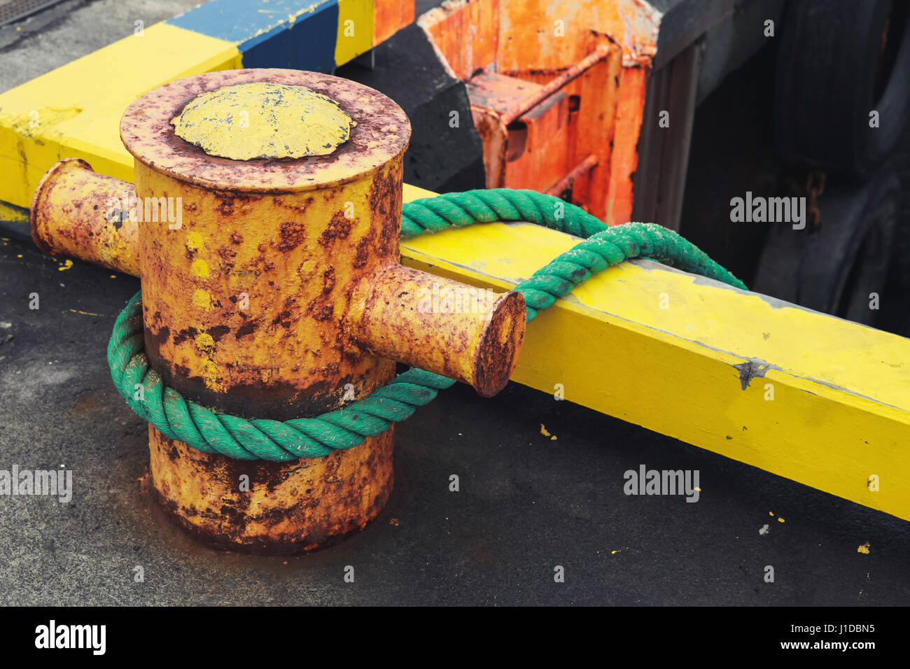 Ships mooring equipment, yellow bollard with ropes mounted in concrete ...