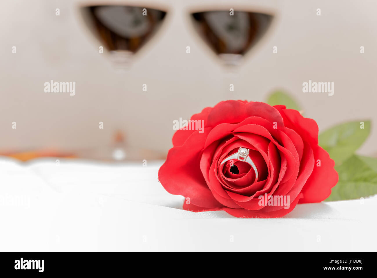 Diamond ring inside red rose over two wine glasses background with copy ...