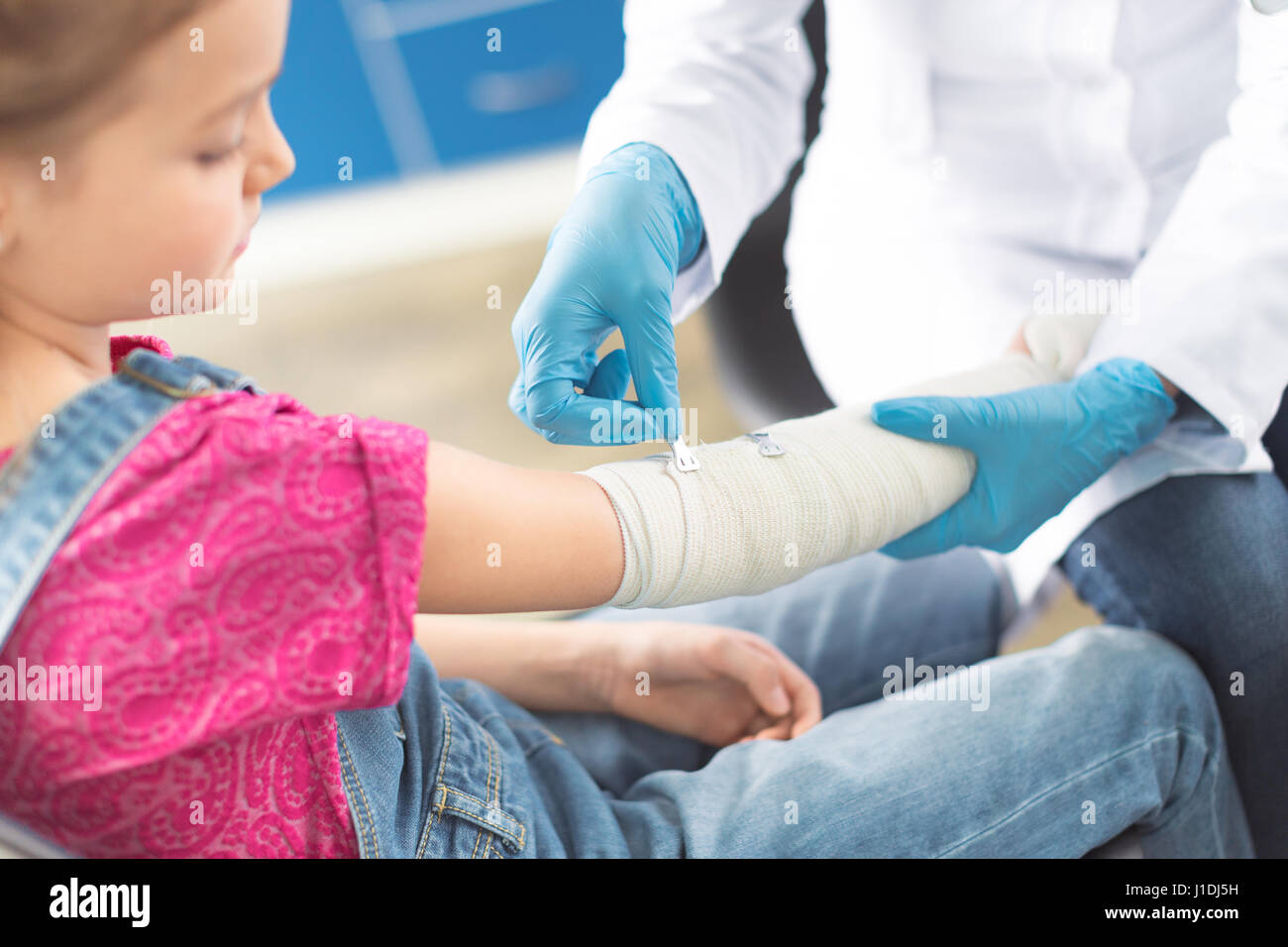 Doctor in white coat and medical gloves bandaging hand of little girl ...