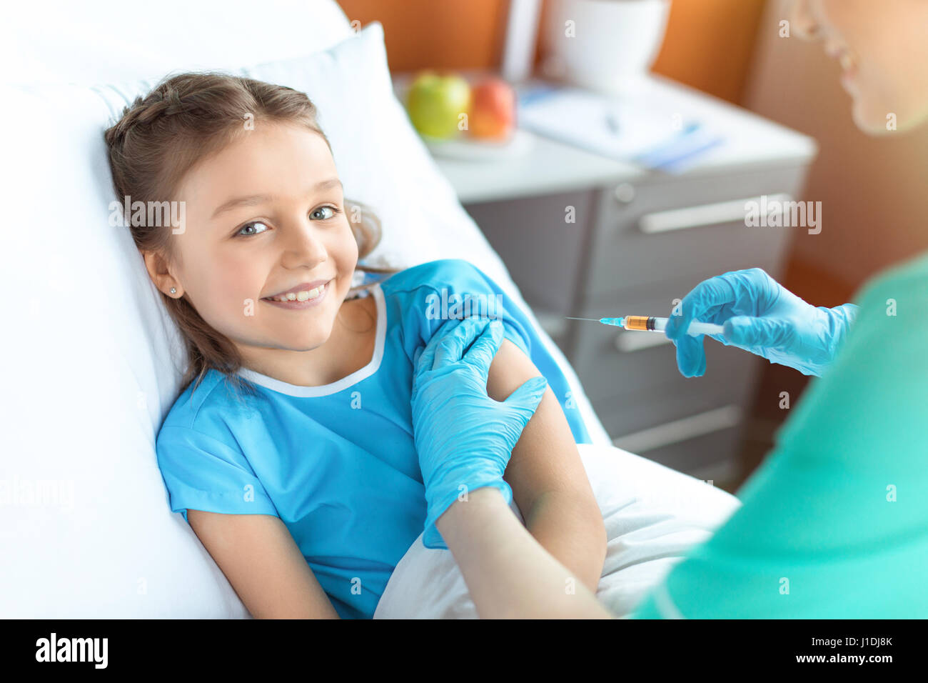 Doctor doing injection to little patient sitting on bed in hospital ...
