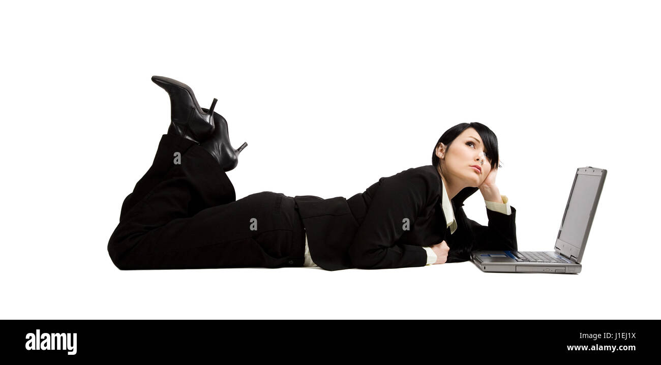 A businesswoman working on her laptop while lying down on the floor ...