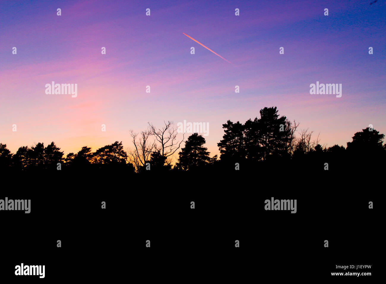 Jet contrail across a beautiful sunset sky over the silhouette of an ...