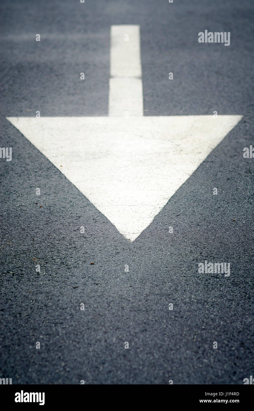 White painted direction arrow sign on asphalt road pointing backwards ...