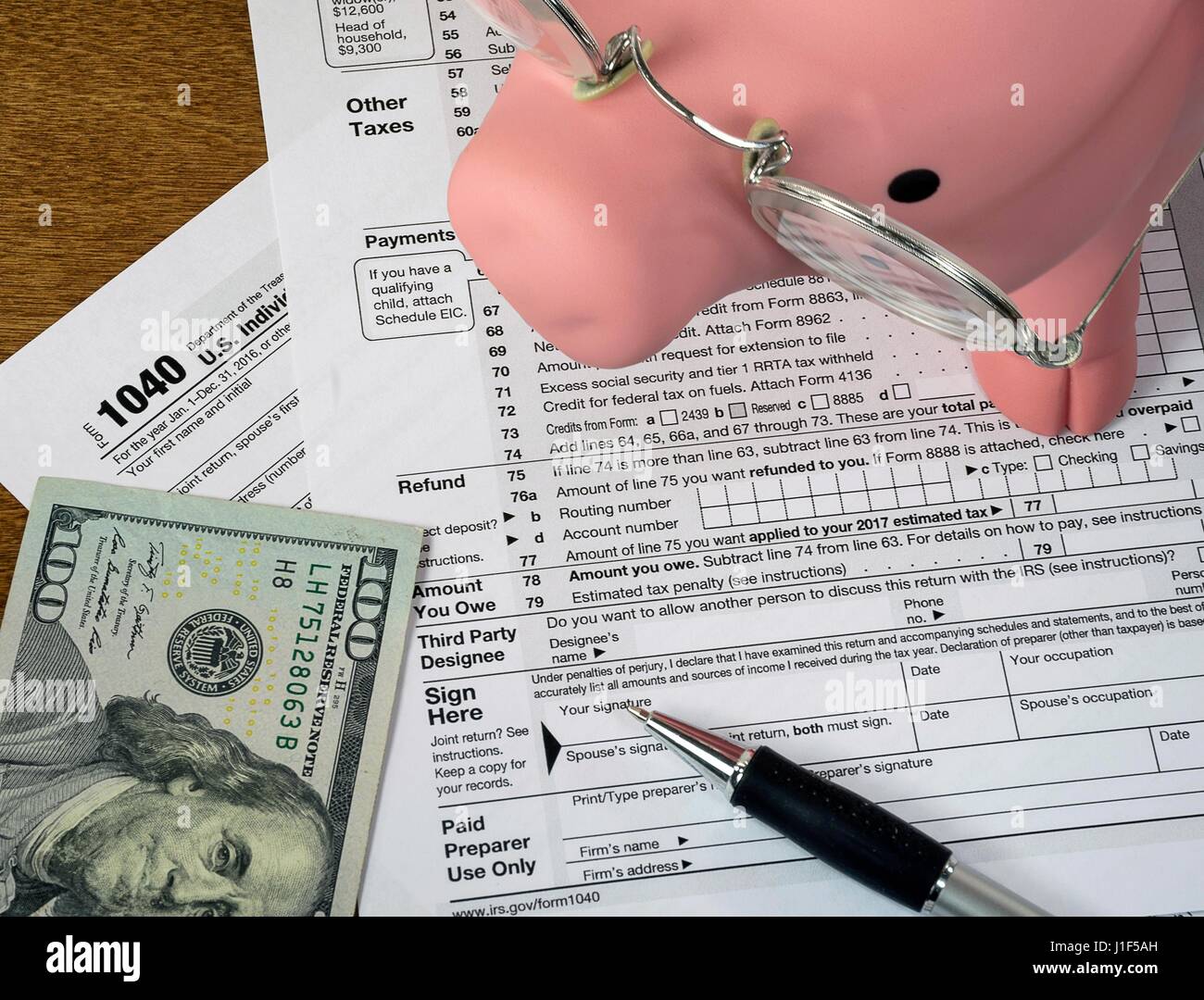 pink piggy bank on income tax form with ink pen and hundred dollar bill ...