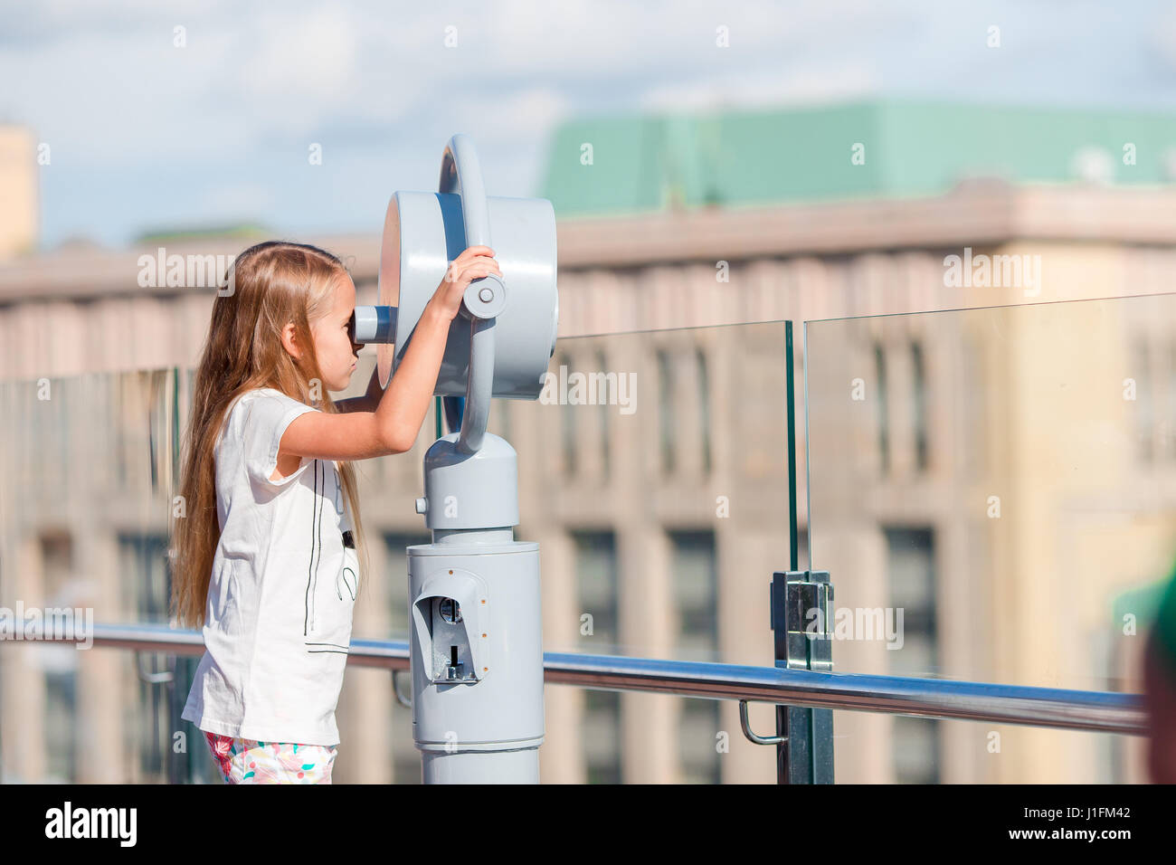 Little girl looking at coin operated binocular on terrace with ...