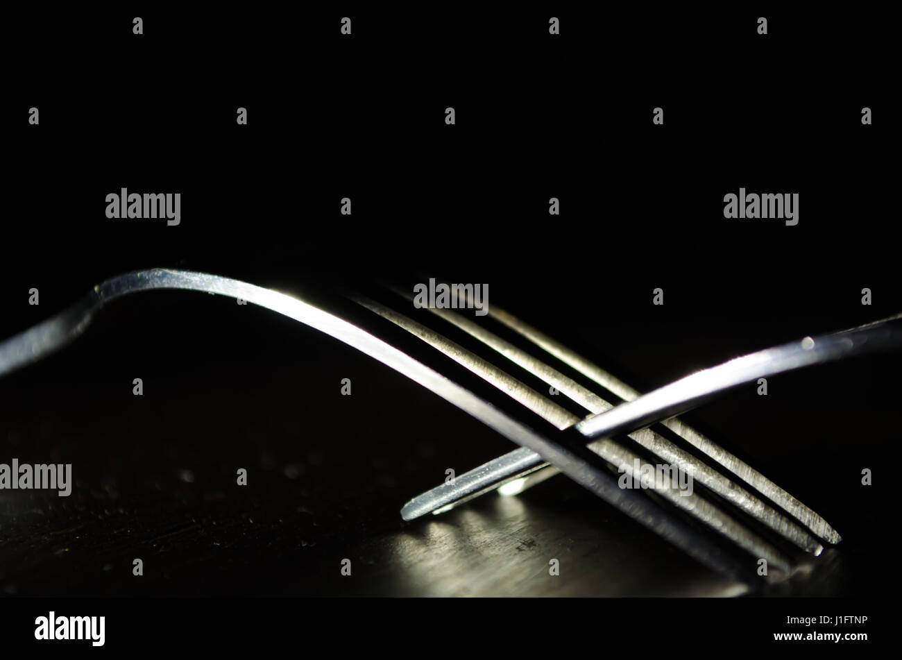 Two mingled steel forks in low key light against dark background Stock ...