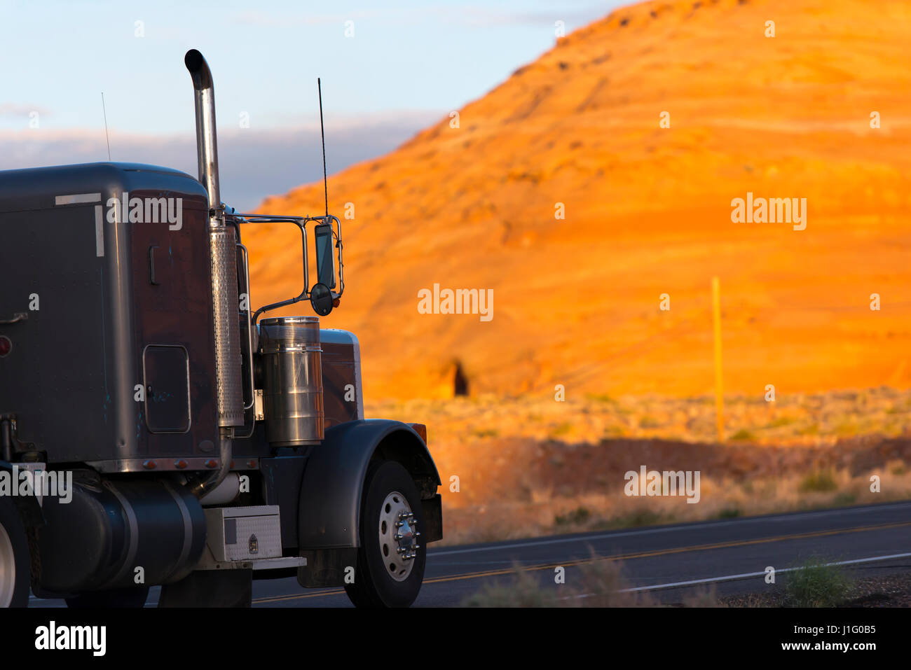 Dark classic big rig semi truck with long exhaust pipes passes by ...