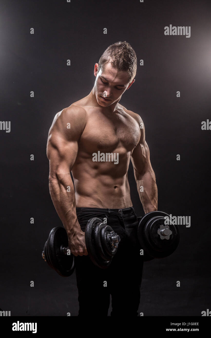 young man bodybuilder looking down holding dumbbells, side view. studio ...