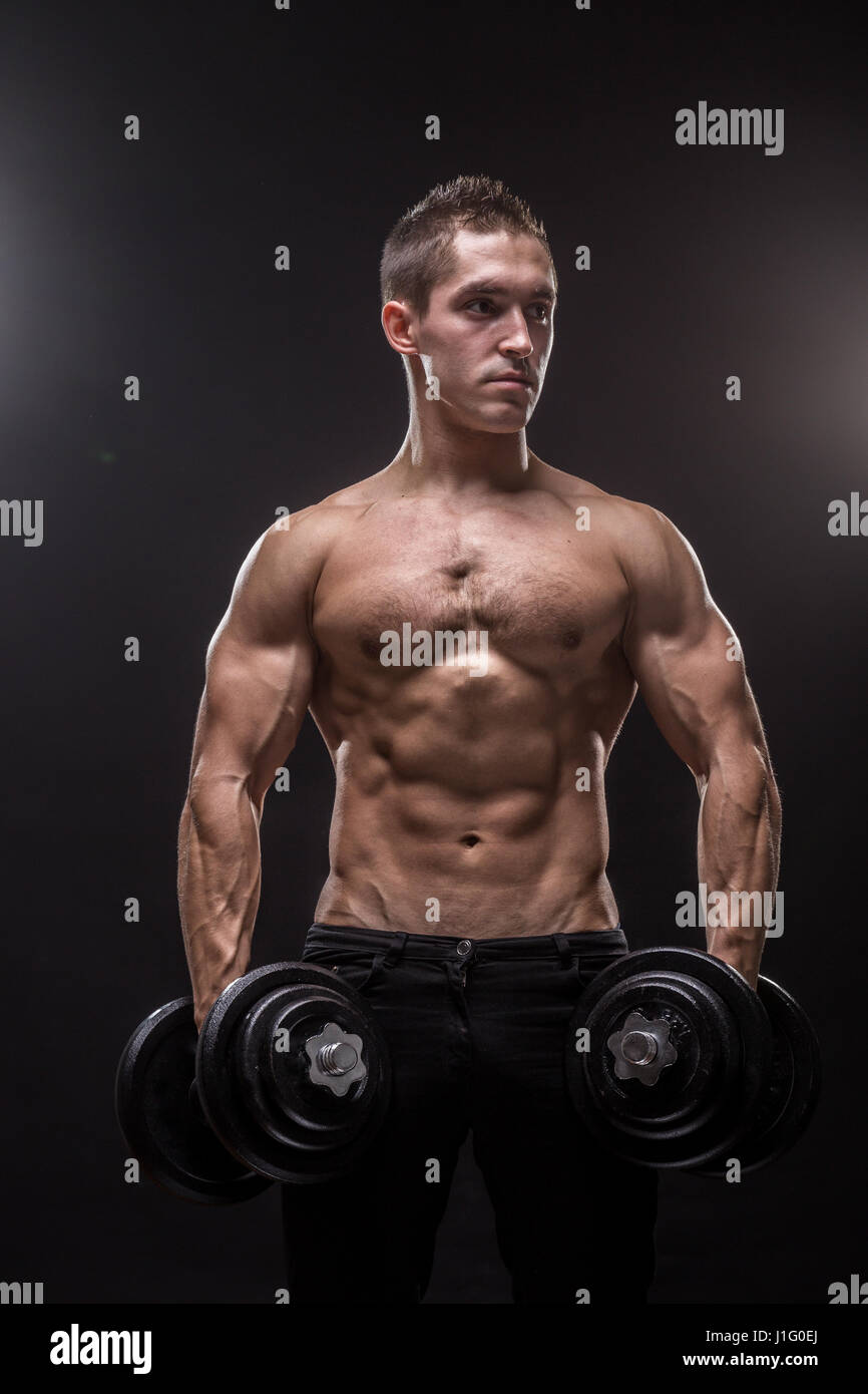 young man bodybuilder looking sideways holding dumbbells. studio ...