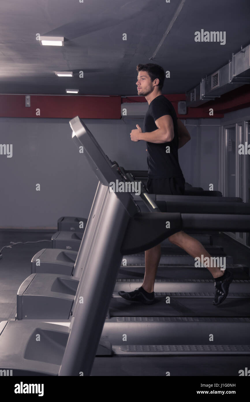 athletic fit slim young man running on treadmill. Many treadmills, line ...
