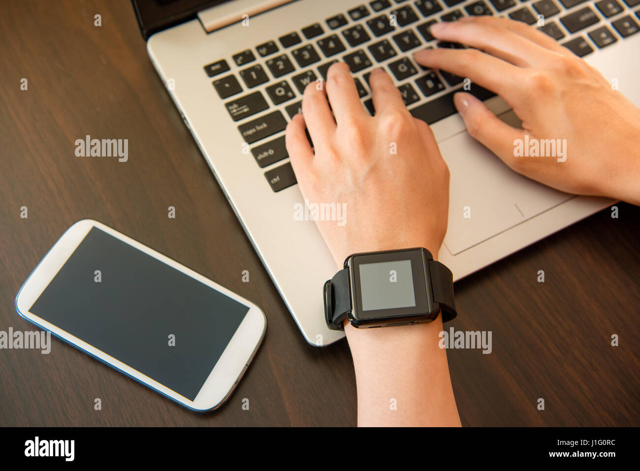 Hands of woman wearing smartwatch on the keyboard of her laptop ...