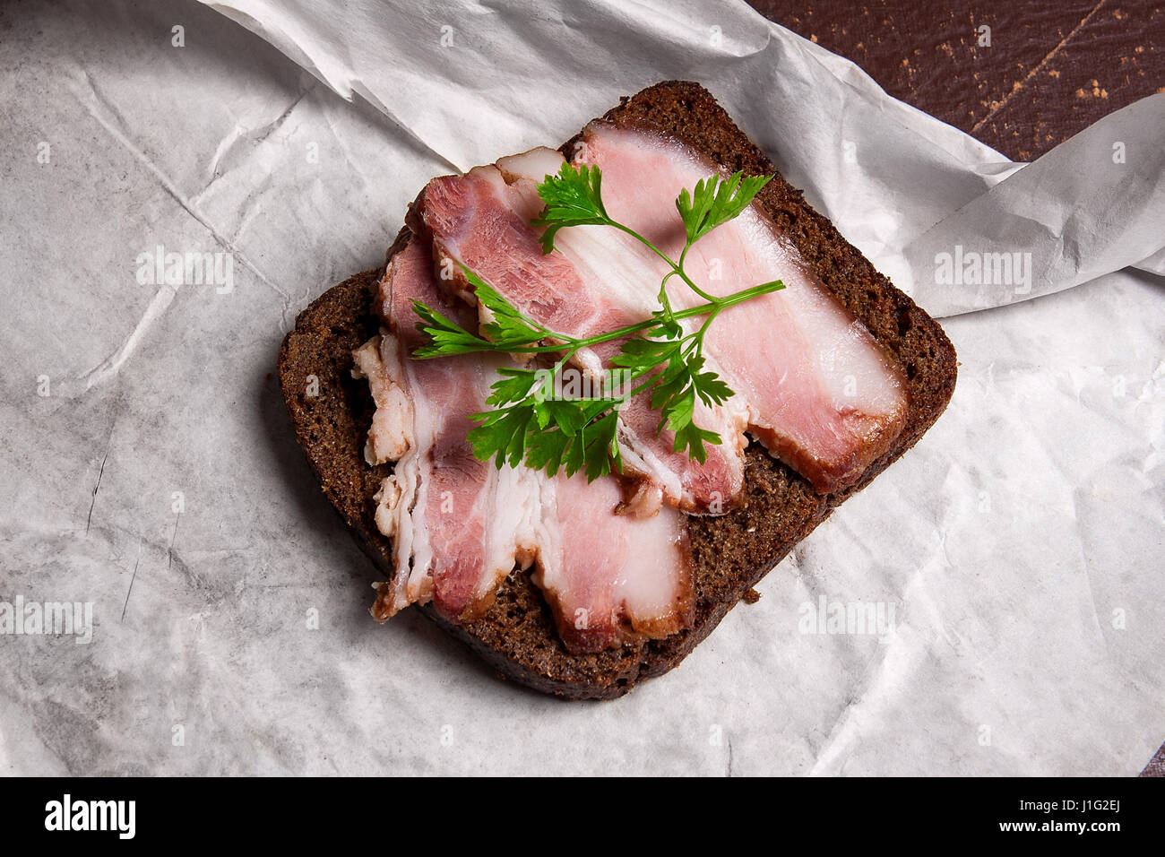 Close up view slices of smoked bacon on the piece rye bread with herbs ...