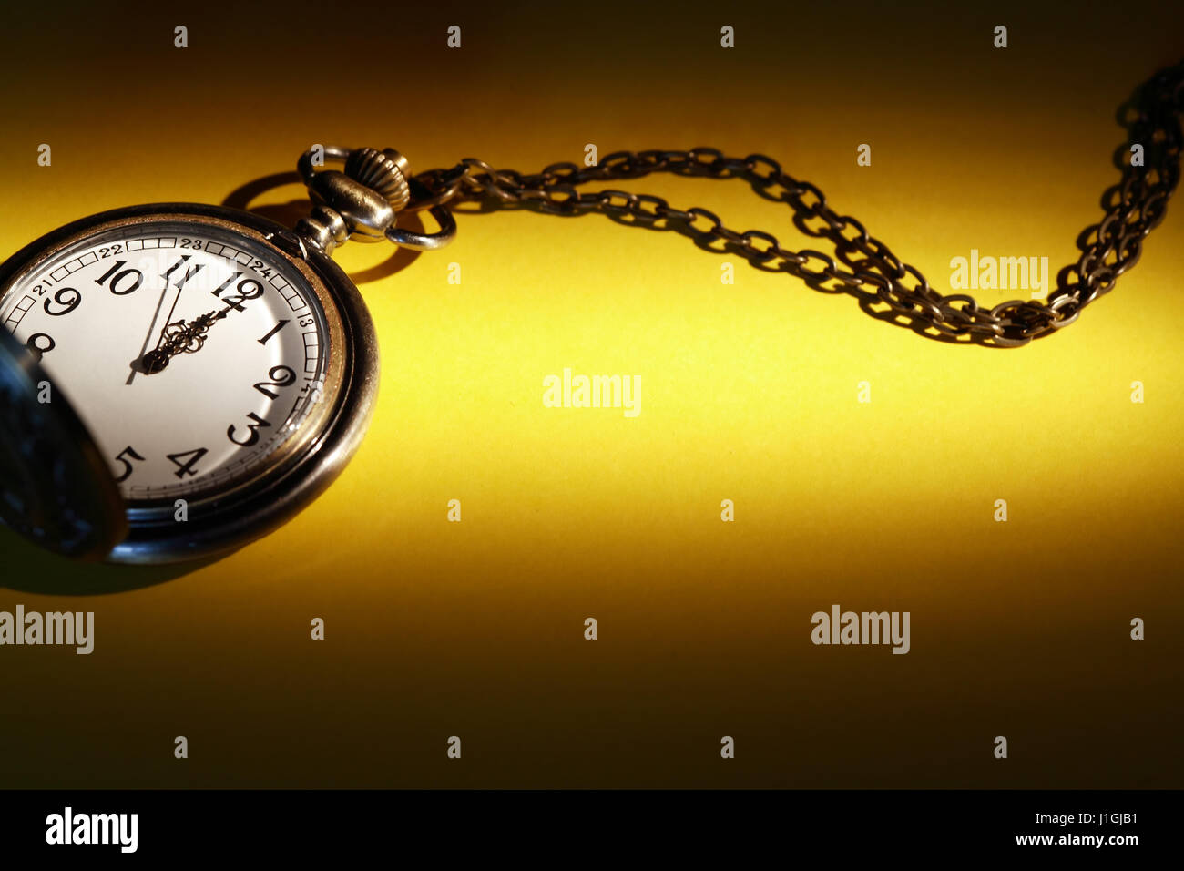 Vintage pocket watch with chain on yellow paper surface under beam of ...